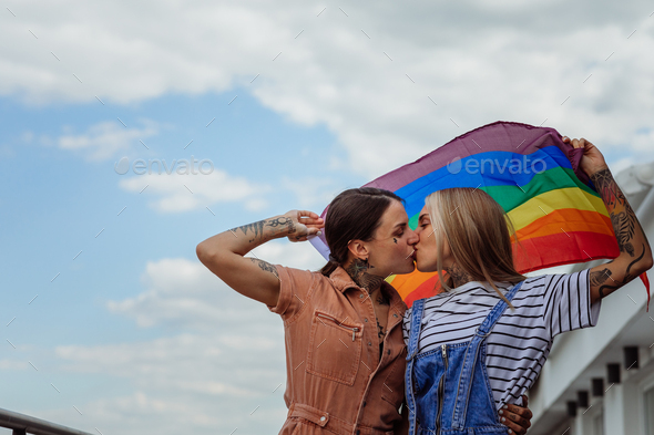 Two lesbian women with rainbow flag kissing Stock Photo by bernardbodo